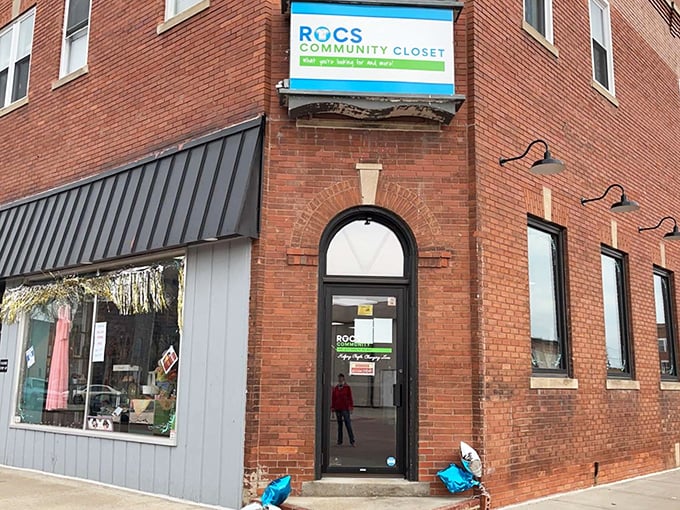 The charming brick facade of ROCS Community Closet welcomes bargain hunters with its distinctive arched doorway and bright blue signage.
