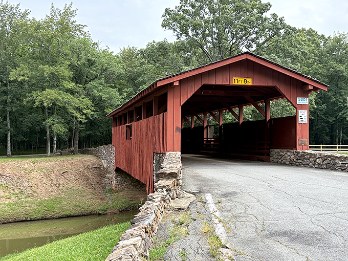 The vibrant red exterior of Burns Park Covered Bridge stands out against Arkansas greenery like a cardinal perched in a pine forest.