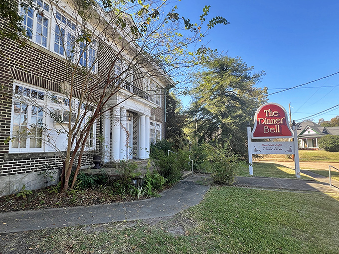The stately brick exterior of The Dinner Bell stands proudly in McComb, its red sign promising Southern comfort without pretension. Home-style dining awaits behind those white columns.