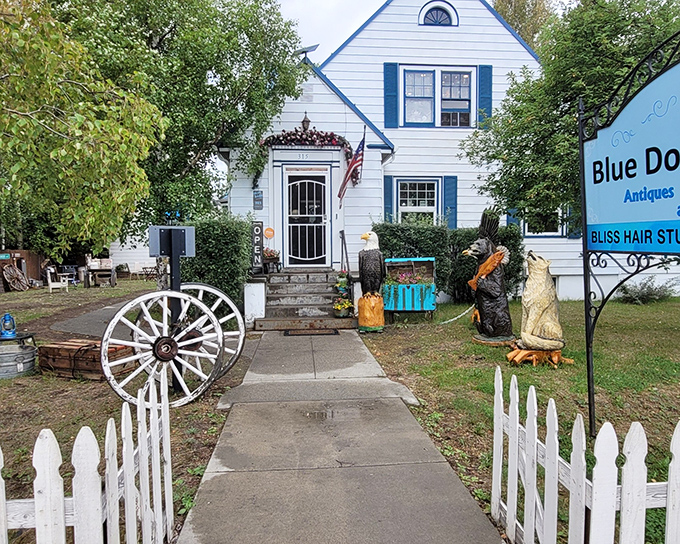A charming white house with a blue door beckons treasure hunters, flanked by carved wooden bears standing guard like the world's most patient greeters.