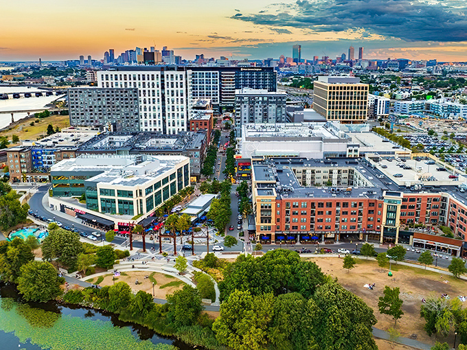 A bird's-eye view of Assembly Row showcasing its perfect blend of shopping, dining, and residential spaces with Boston's skyline glimmering in the distance.