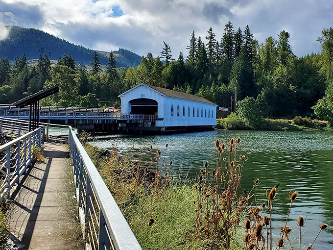 
The classic white facade of Lowell Covered Bridge stands like a portal to simpler times, inviting visitors to step through history while wildflowers dance in the foreground.