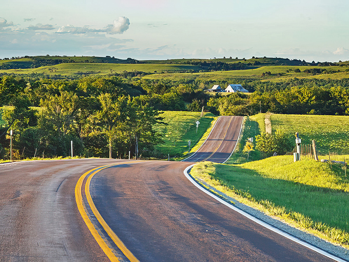 The road ahead curves like a promise, inviting you into the undulating emerald embrace of Kansas's hidden treasure.