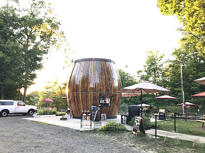 The Root Beer Barrel stands like a wooden sentinel at dusk, its warm amber hues glowing in the evening light while umbrellas create cozy outposts for root beer enthusiasts.