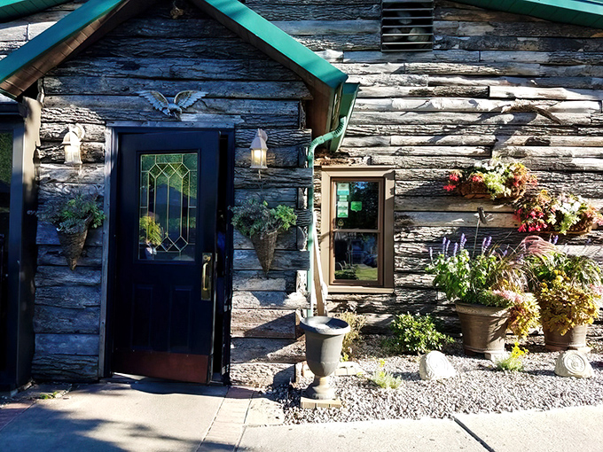 The rustic log cabin exterior of The Whitehouse Inn beckons like a woodland fairy tale, complete with stained glass door and seasonal flower displays.