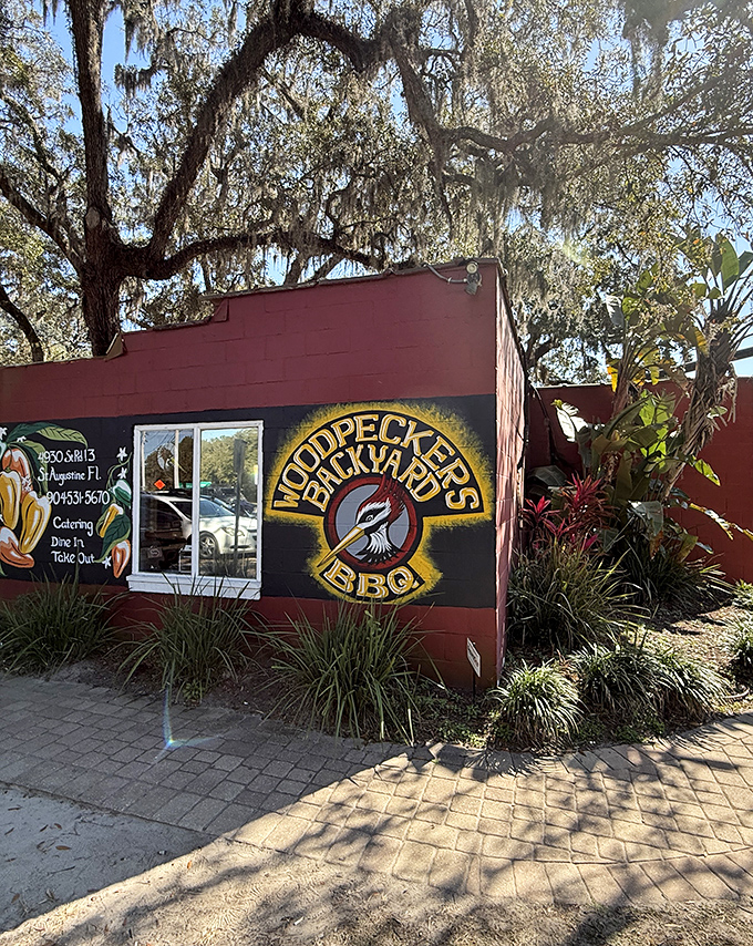 Spanish moss drapes over this unassuming BBQ sanctuary like nature's own welcome banner. The bright woodpecker logo promises what the building delivers: flavor with character.