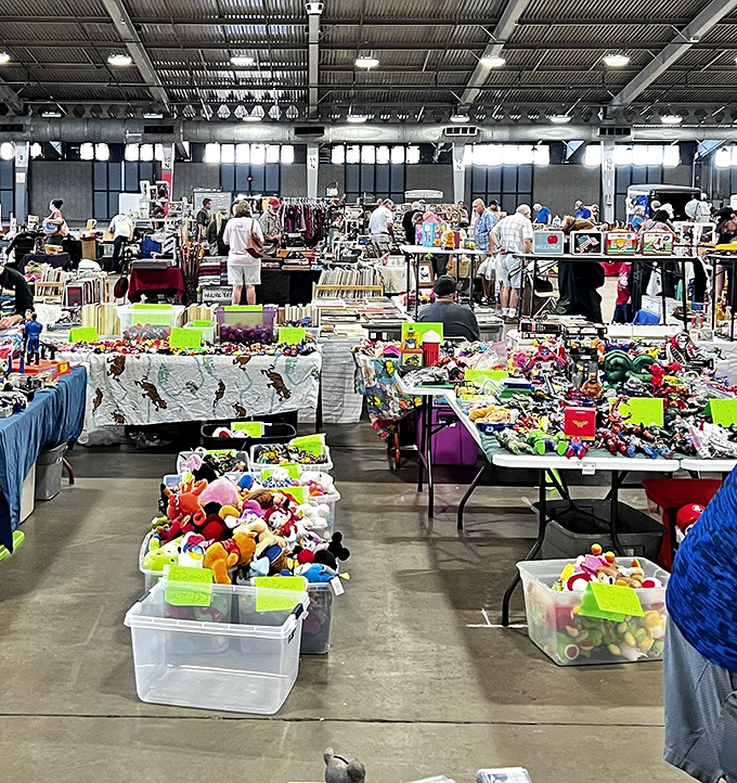 A treasure hunter's paradise unfolds under industrial lighting, where tables overflow with potential finds and shoppers navigate the labyrinth of possibilities.