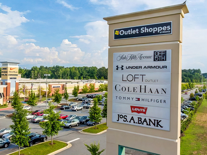 The grand entrance sign showcases premium brands that await inside, standing like a fashionable sentinel guarding a kingdom of discounts and designer dreams.
