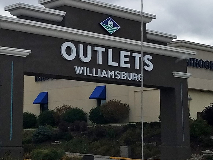 The grand entrance to Outlets Williamsburg stands like a retail Stonehenge, beckoning shoppers with promises of treasures within.