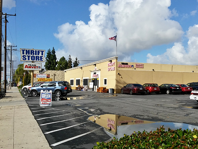 The unassuming exterior of AMVETS Thrift Store in Long Beach stands like a treasure chest waiting to be opened, complete with American flag proudly waving above.