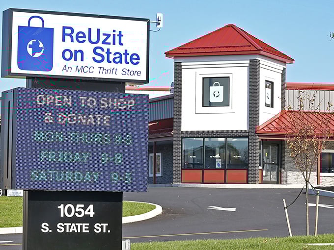 The welcoming entrance to ReUzit on State, with its distinctive red roof and digital sign displaying generous shopping hours for bargain hunters.