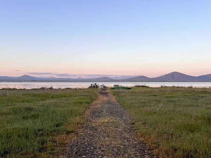 A gravel path leads to tranquil waters at sunset, where mountains frame the horizon like nature's own theater backdrop. This is California's invitation to adventure.
