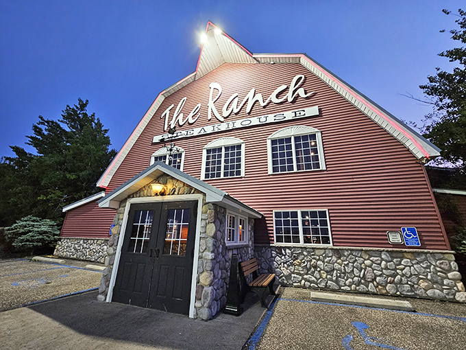 The iconic barn-shaped exterior of The Ranch Steakhouse glows with promise at dusk, like a beacon of culinary comfort in Devils Lake.