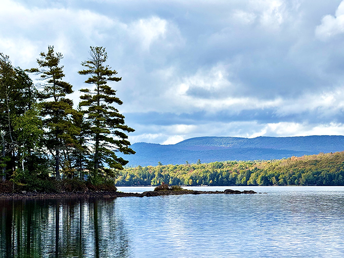 Nature's perfect mirror act &ndash; towering pines stand sentinel on a rocky peninsula while distant mountains create the backdrop for Umbagog's crystal waters.