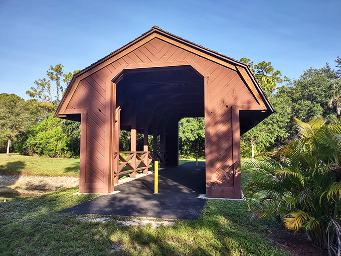 Barn-red and beautiful, the covered bridge's entrance frames the lush greenery beyond, promising a moment of rustic tranquility.