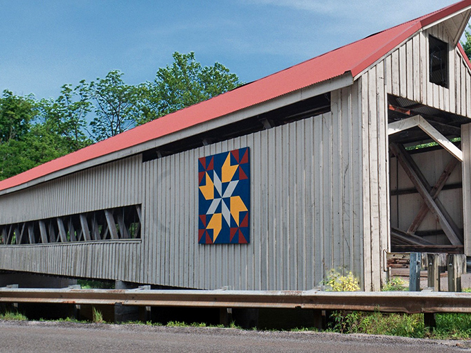 The iconic white siding and crimson roof of Mechanicsville Bridge stand out like architectural candy against Ohio's blue sky, complete with a colorful quilt square that tells its own story.
