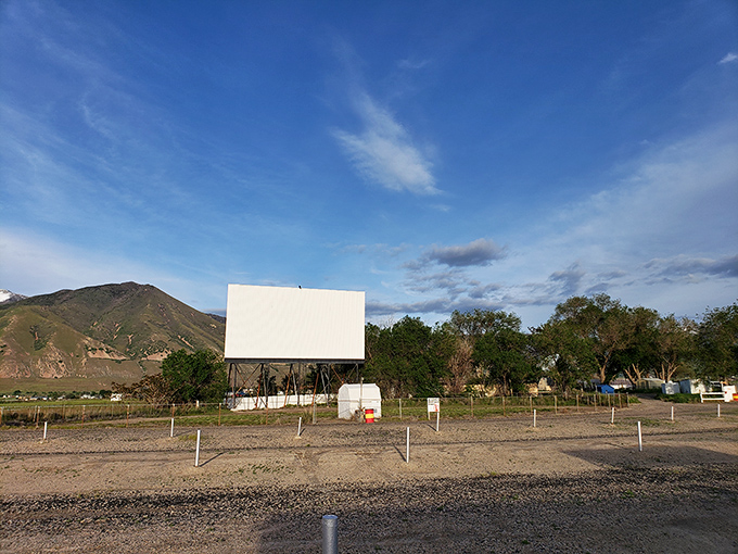 The iconic white screen of Erda Drive-In stands proudly against Utah's majestic Oquirrh Mountains, like a canvas awaiting twilight's cinematic magic.