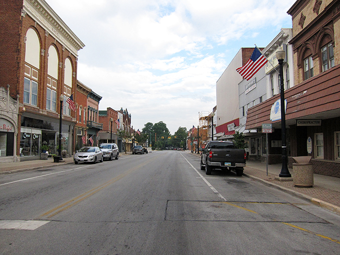 Auglaize Street stretches into the distance, American flags fluttering above storefronts that have witnessed decades of small-town life.