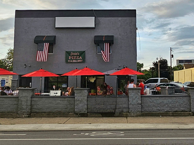 The gray exterior might not scream "culinary destination," but those red umbrellas and American flags hint at the unpretentious deliciousness waiting inside Josie's Pizza.