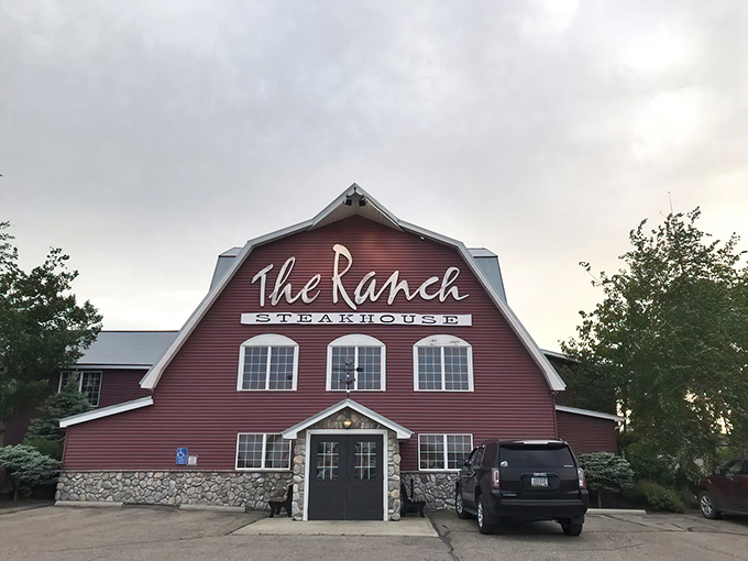 The iconic barn-shaped exterior of The Ranch Steakhouse glows with promise at dusk, like a beacon of culinary comfort in Devils Lake.