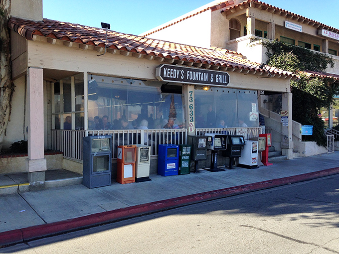 The unassuming exterior of Keedy's Fountain & Grill stands as a time capsule in Palm Desert, complete with vintage newspaper boxes that remind us life existed before smartphones.