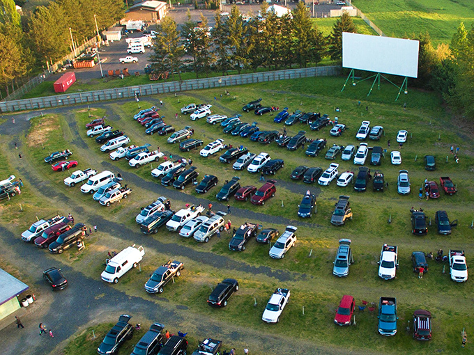 A bird's-eye view of cinematic paradise! Cars arranged in perfect rows facing the massive white screen, like a drive-up congregation worshipping at the altar of film.
