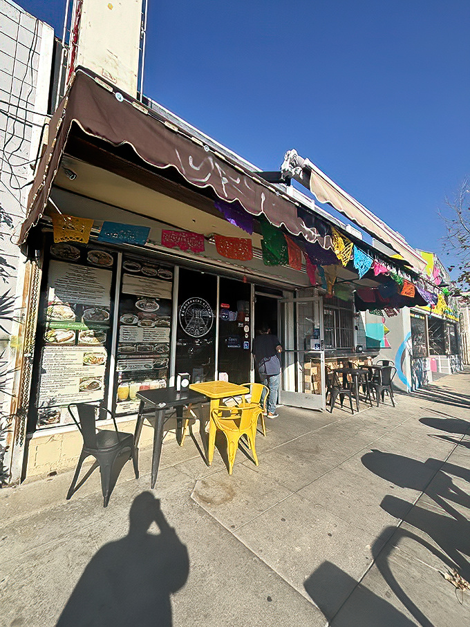 Colorful papel picado banners dance overhead while simple outdoor seating invites passersby to pause for a taste of Mexico in Los Angeles.