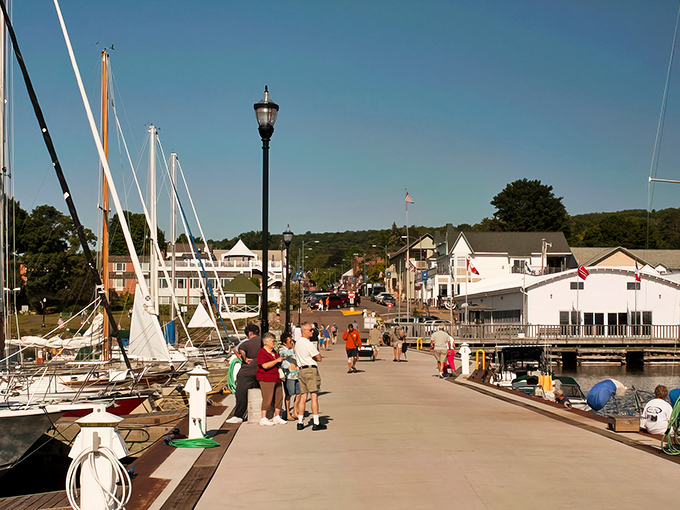 The marina boardwalk buzzes with summer energy as sailboats stand at attention like eager students waiting to be called to adventure.