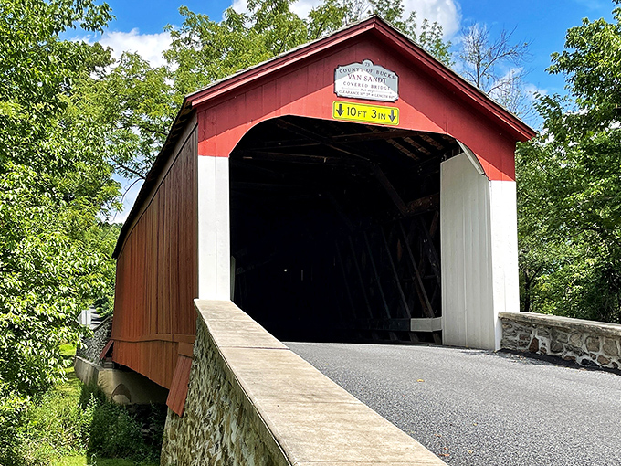 The classic red exterior of Van Sant Covered Bridge stands as a vibrant sentinel against Pennsylvania's lush greenery, a postcard-perfect scene from another era.
