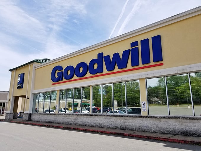 The bright blue Goodwill sign beckons like a lighthouse for bargain hunters. Behind those windows lie treasures waiting to be discovered.