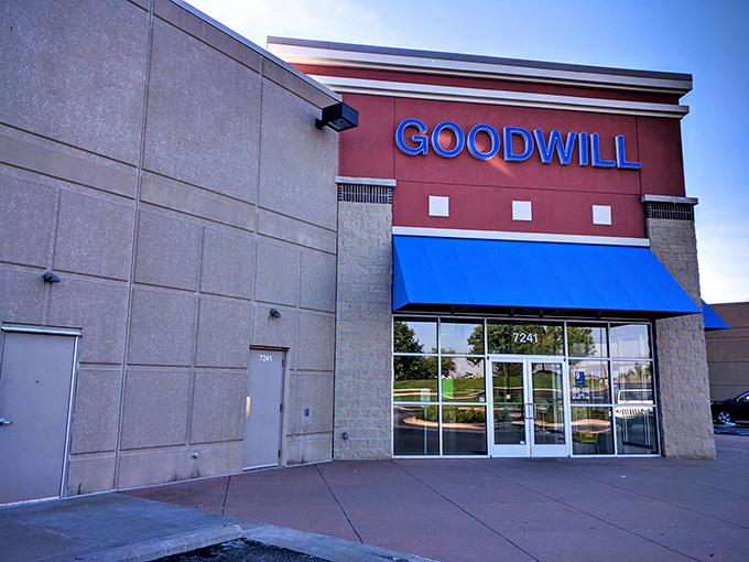 The Goodwill storefront stands proud in Overland Park, its blue awning beckoning like a thrift oasis in a retail desert of sameness.