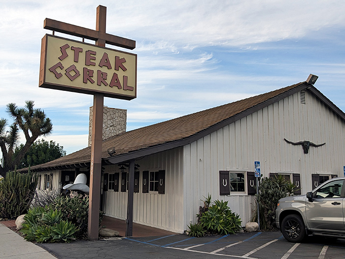 The iconic Steak Corral sign stands tall against the California sky, promising carnivorous delights within its unassuming ranch-style building.