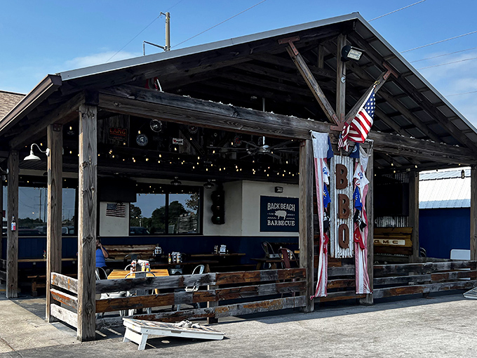 The rustic wooden exterior of Back Beach Barbecue beckons like a smoke signal to hungry souls. That American flag isn't just decoration&mdash;it's a promise of classic American comfort food done right.