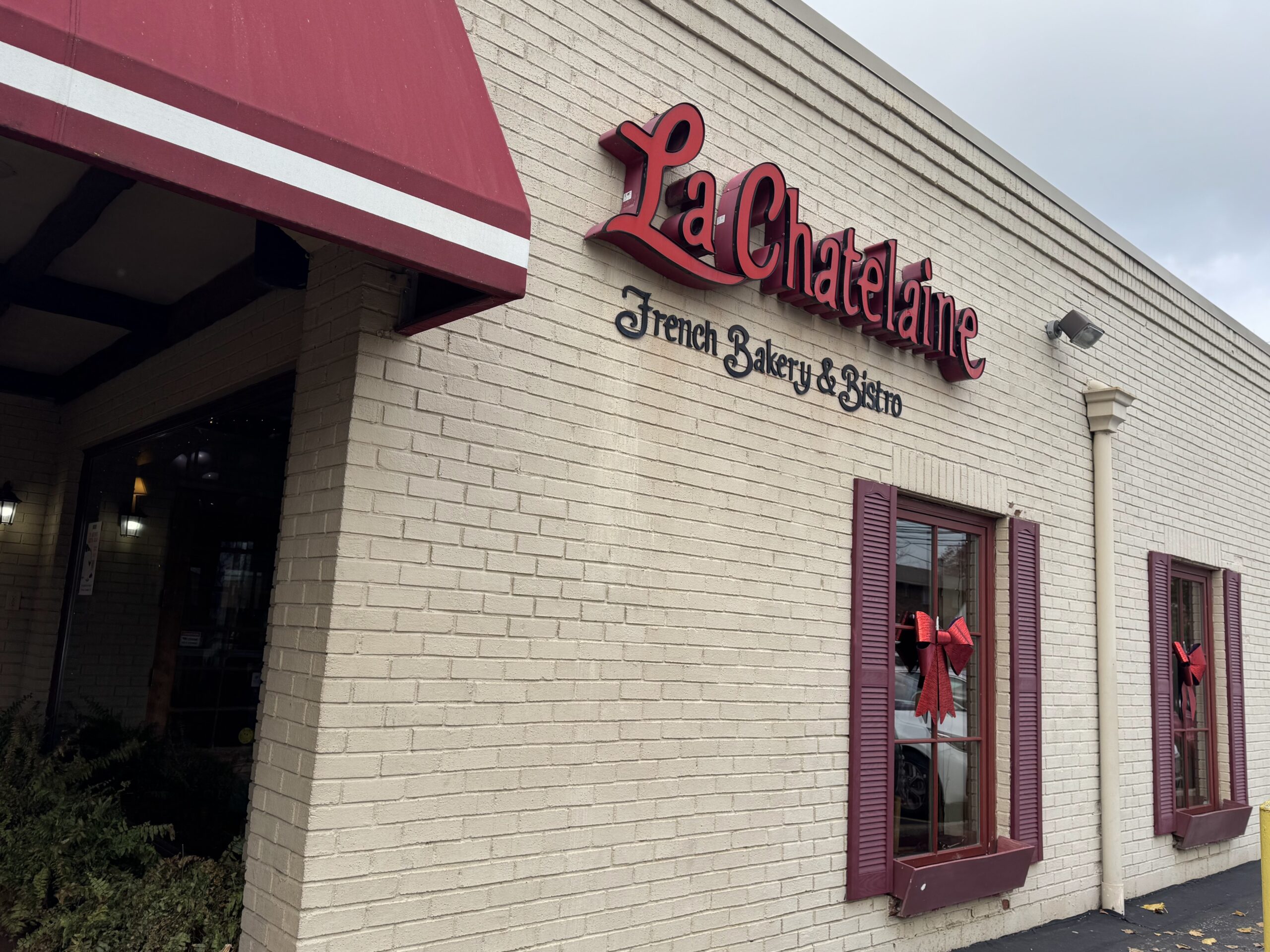 The iconic red signage of La Chatelaine against cream-colored brick promises French delights that deliver on every syllable of "authentique."
