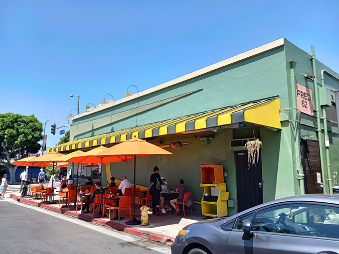 Fred 62's mint-green exterior with yellow-striped awnings stands like a retro time capsule on Vermont Avenue, where outdoor diners soak up sunshine and people-watching opportunities under cheerful orange umbrellas.