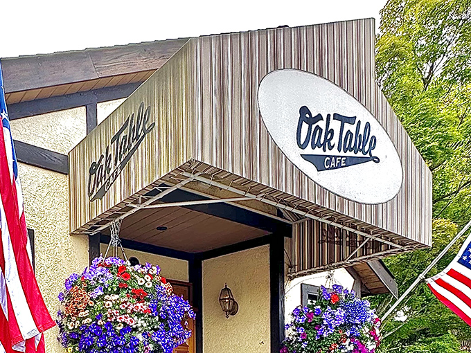 The charming exterior of Oak Table Cafe welcomes you with vibrant hanging flower baskets and American flags, promising comfort before you even step inside.