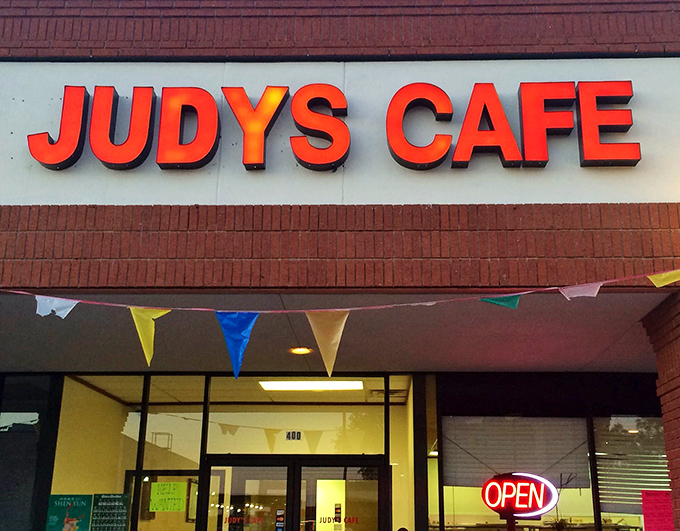The bright red lettering of Judy's Cafe beckons like a lighthouse for the hungry, promising homestyle comfort beneath cheerful bunting flags.