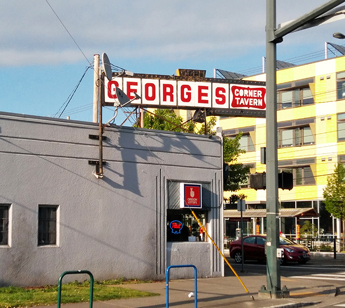 The iconic red sign beckons like a lighthouse for the hungry. George's Corner Tavern stands proudly against Portland's modern backdrop, promising comfort in every bite.