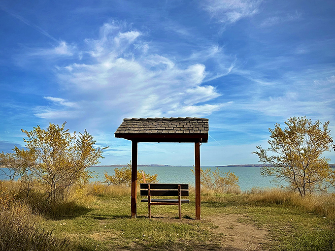 A solitary bench under a rustic shelter offers front-row seats to Lake Sakakawea's vast beauty. Nature's therapy office, no appointment necessary.