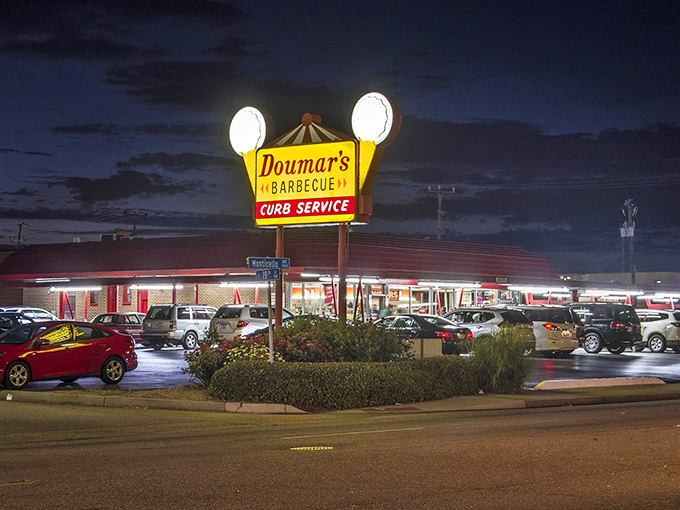 The iconic Doumar's sign glows like a beacon in the night, promising curb service and barbecue that's been drawing crowds since before color TV existed.
