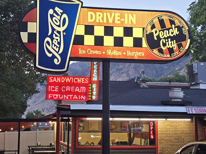 The iconic Peach City sign stands like a neon lighthouse, guiding hungry travelers to a promised land of milkshakes and burgers against the backdrop of Utah mountains.