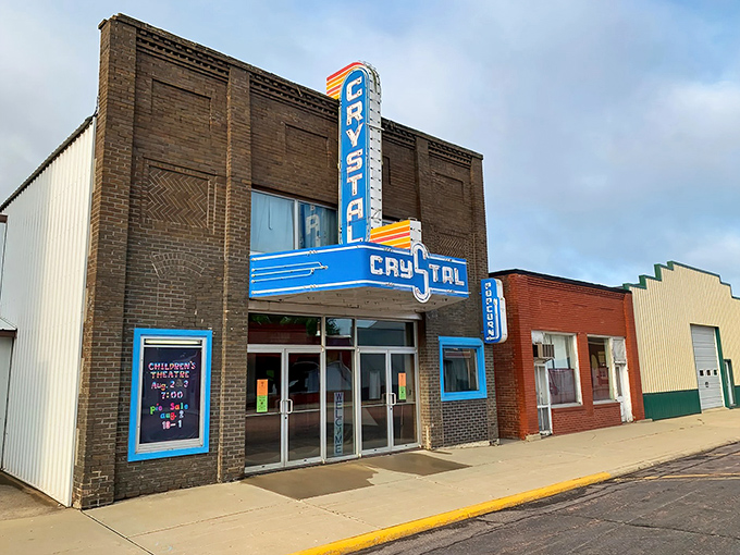 The Crystal Theatre's neon sign cuts through prairie darkness like a beacon, promising movie magic in this digital age.