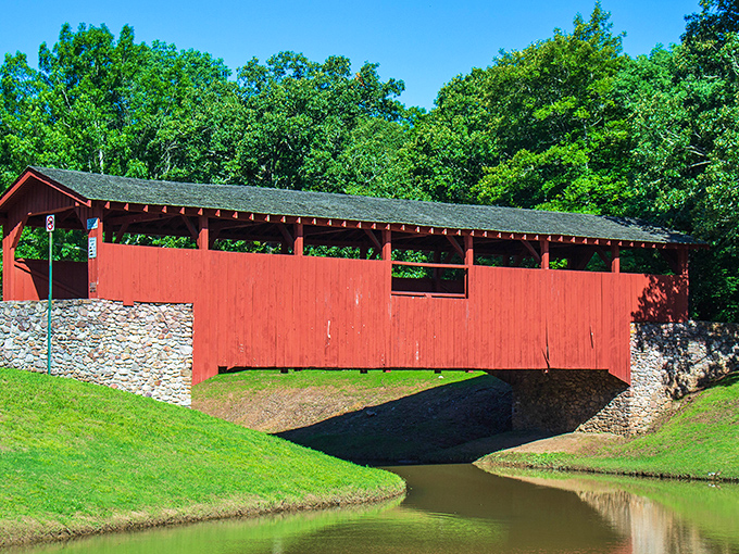 The vibrant red exterior of Burns Park Covered Bridge stands out against Arkansas greenery like a cardinal perched in a pine forest.