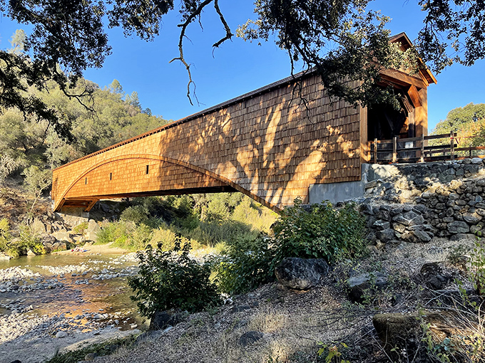 The honey-hued Bridgeport Covered Bridge stretches across the South Yuba River like a wooden time capsule, its weathered shingles glowing in the California sunshine.