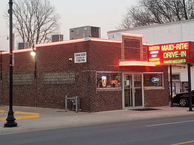 The neon glow of Maid-Rite's sign has been beckoning hungry travelers since 1934, a brick-and-mortar time machine serving comfort on a bun. 