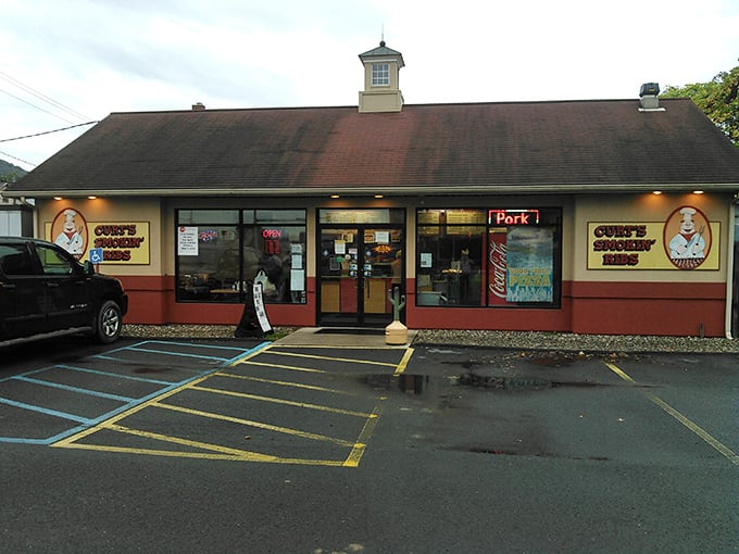 The unassuming exterior of Curt's Smokin' Ribs in Mill Hall, with its distinctive red trim and cartoon chef logo, belies the barbecue magic inside.
