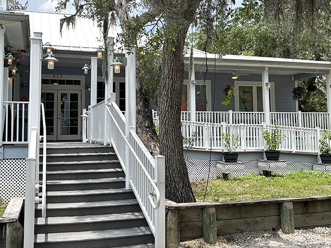 The welcoming entrance to Aunt Kate's, where Spanish moss-draped trees frame the charming coastal building with its inviting porch.