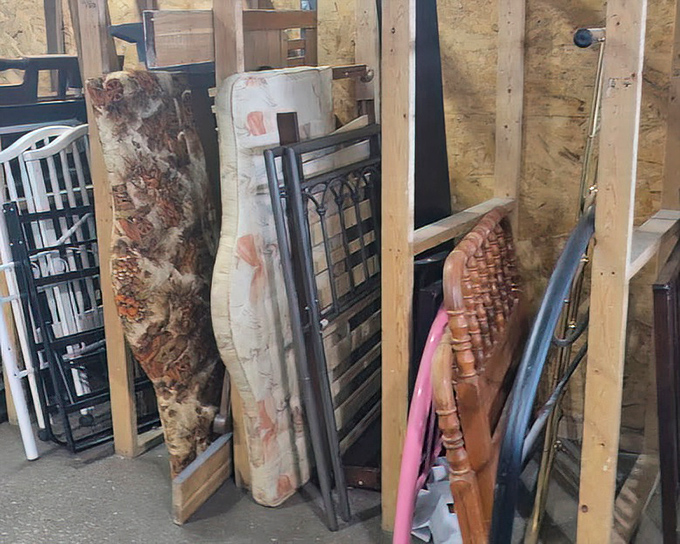 Bedroom furniture leans patiently against wooden dividers, each headboard and frame dreaming of becoming the centerpiece in someone's sanctuary.