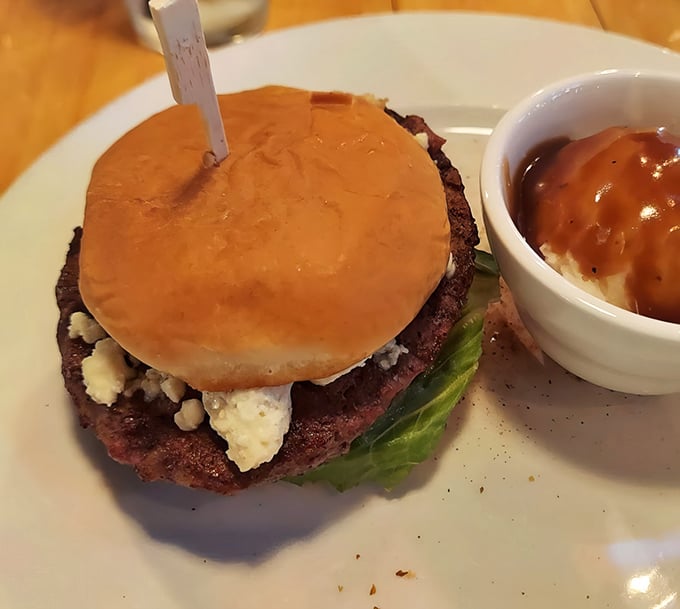 A burger that means business, topped with what appears to be blue cheese on a perfectly toasted bun. The side of mashed potatoes looks equally comforting.