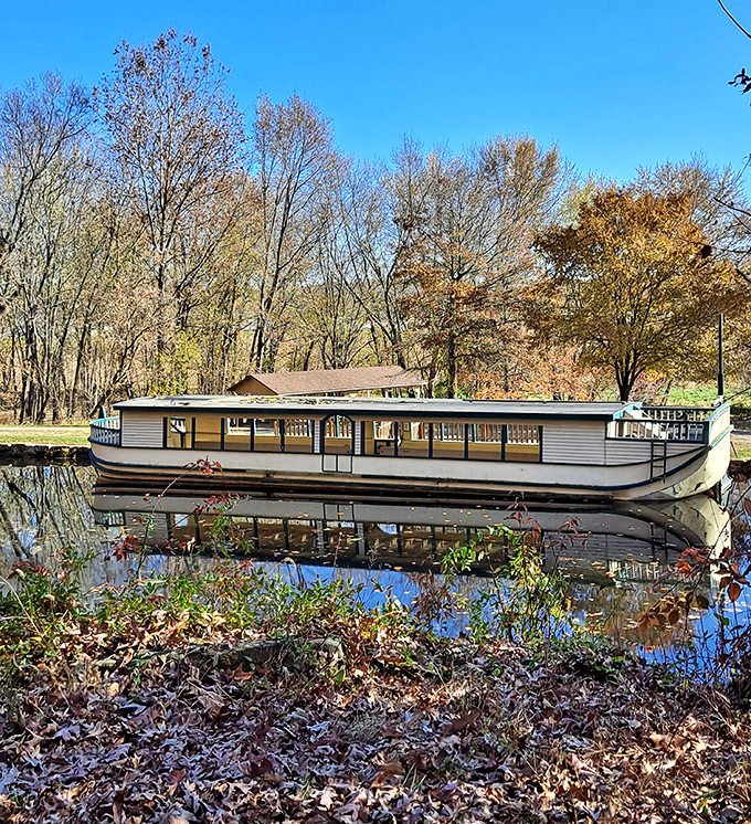 The Monticello III canal boat sits perfectly still, mirrored in water that remembers a time when "shipping" meant actual boats, not clicking buttons online.